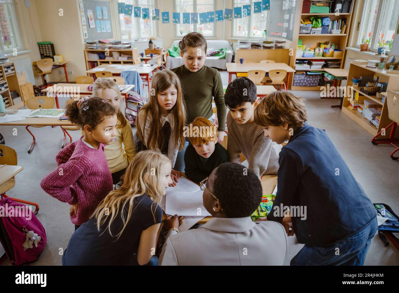 Students looking at teacher helping them in classroom Stock Photo - Alamy