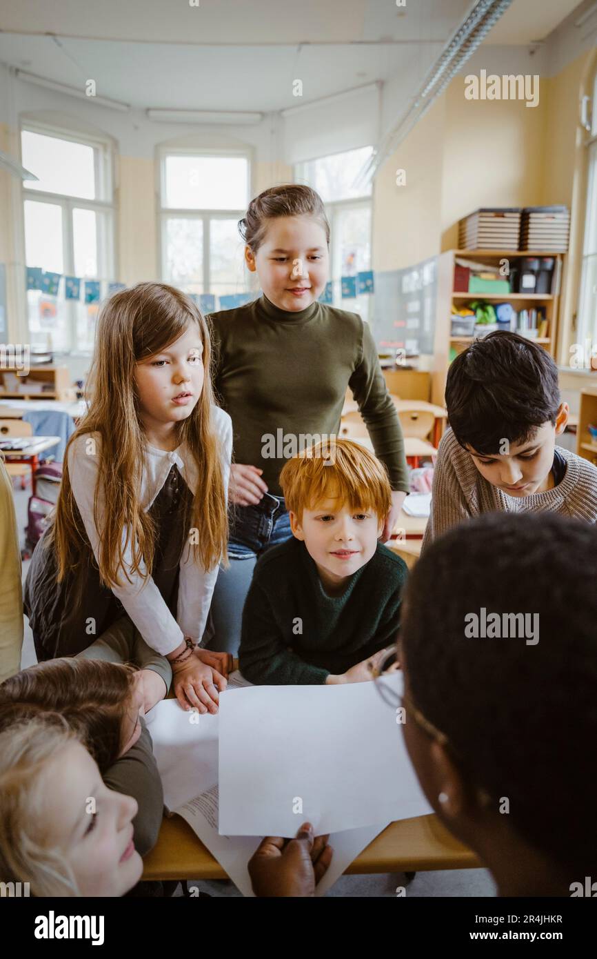 Boys and girls looking at teacher helping them in classroom Stock Photo ...