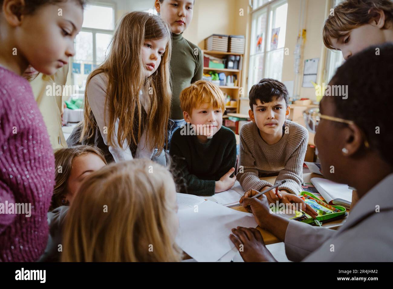 Boys and girls looking at teacher explaining in classroom at elementary ...