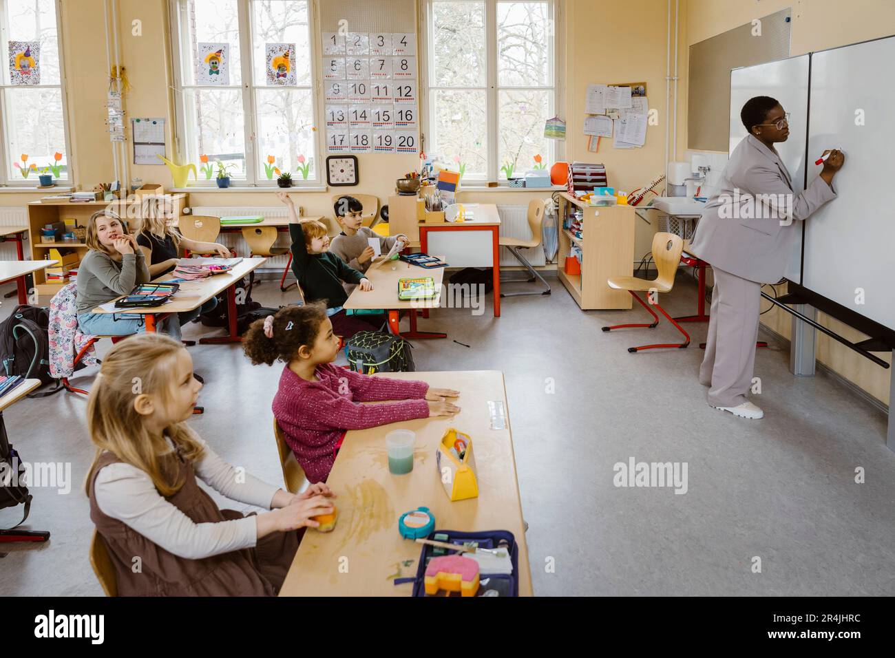 Students looking at teacher writing on whiteboard in classroom Stock ...