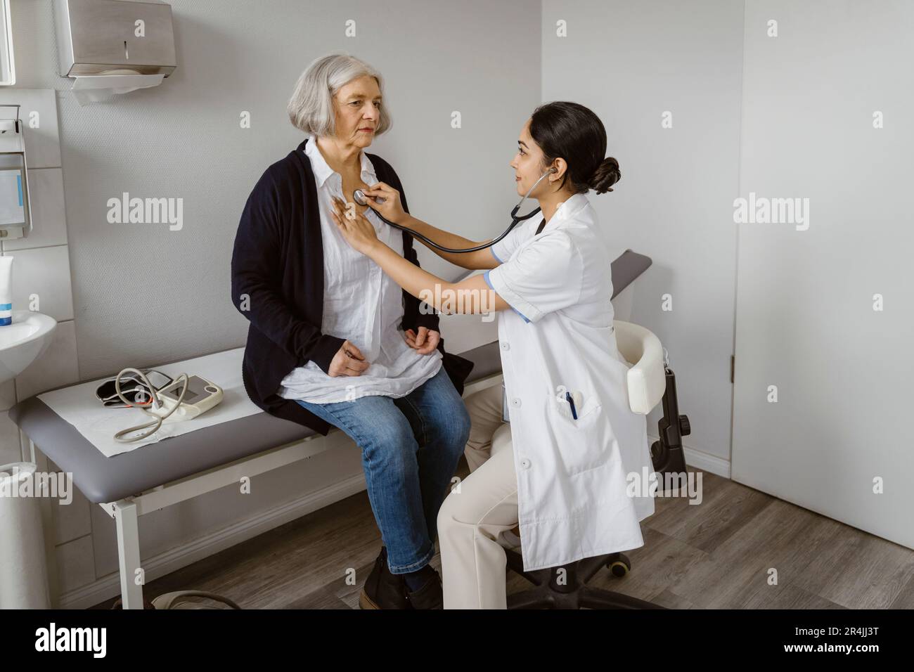 Side view of female doctor listening heartbeat of senior patient ...