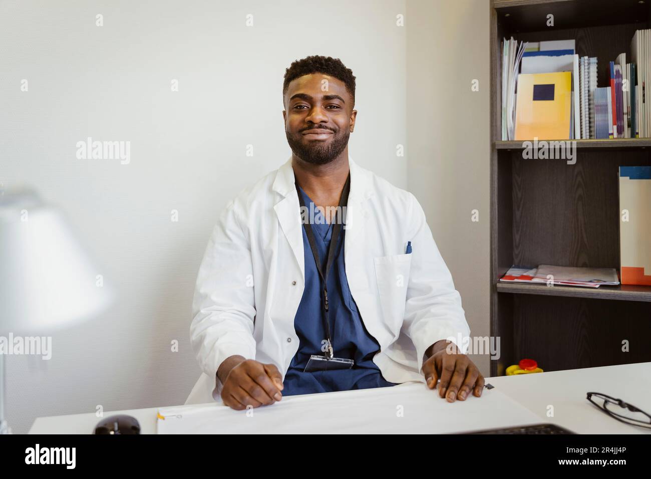 Portrait of smiling male healthcare worker wearing lab coat sitting at ...