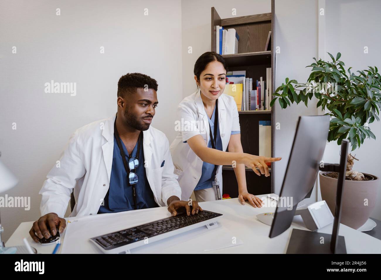 Female doctor explaining male colleague over computer at desk in clinic ...