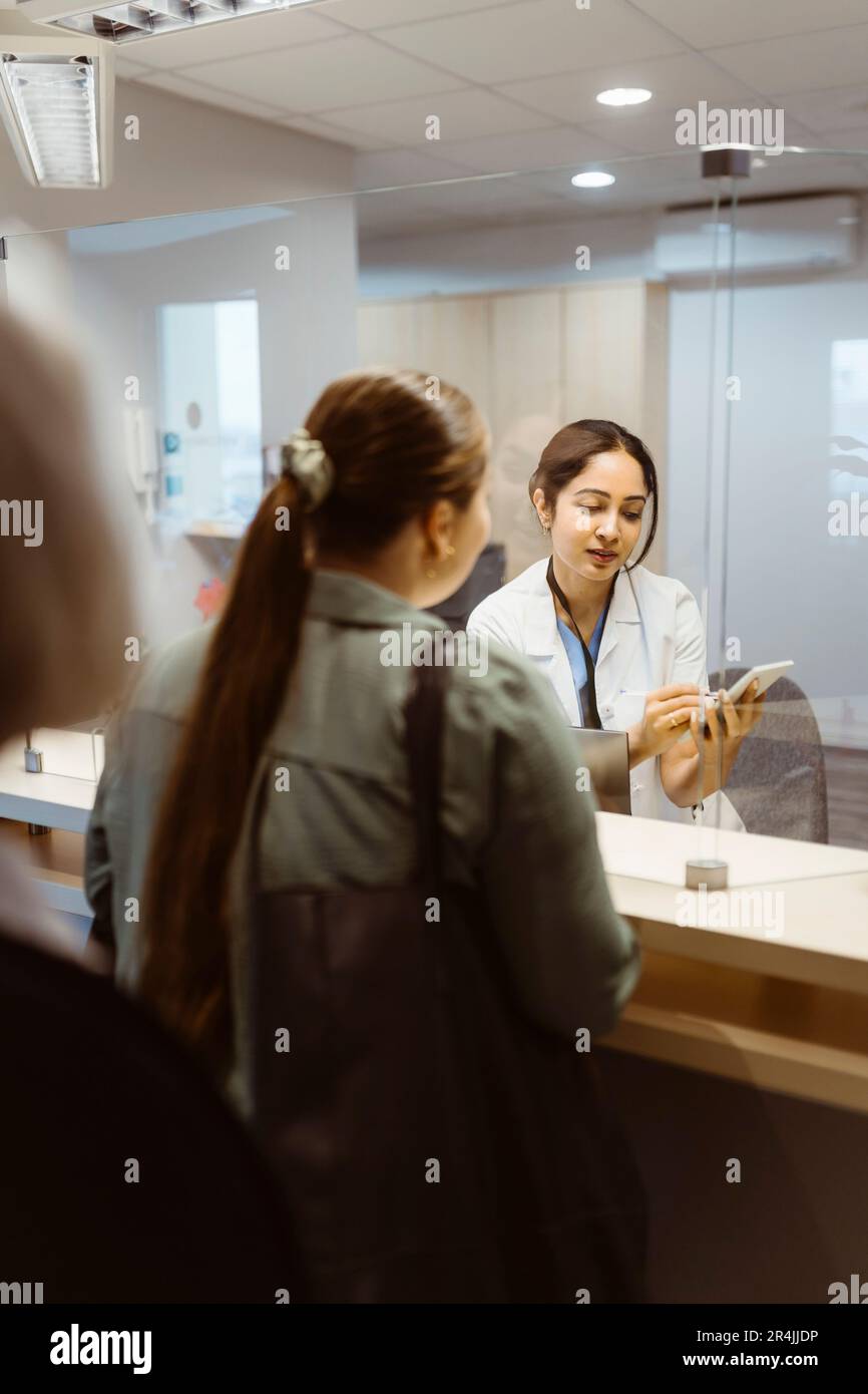 Receptionist registering female patient name in tablet PC at hospital ...