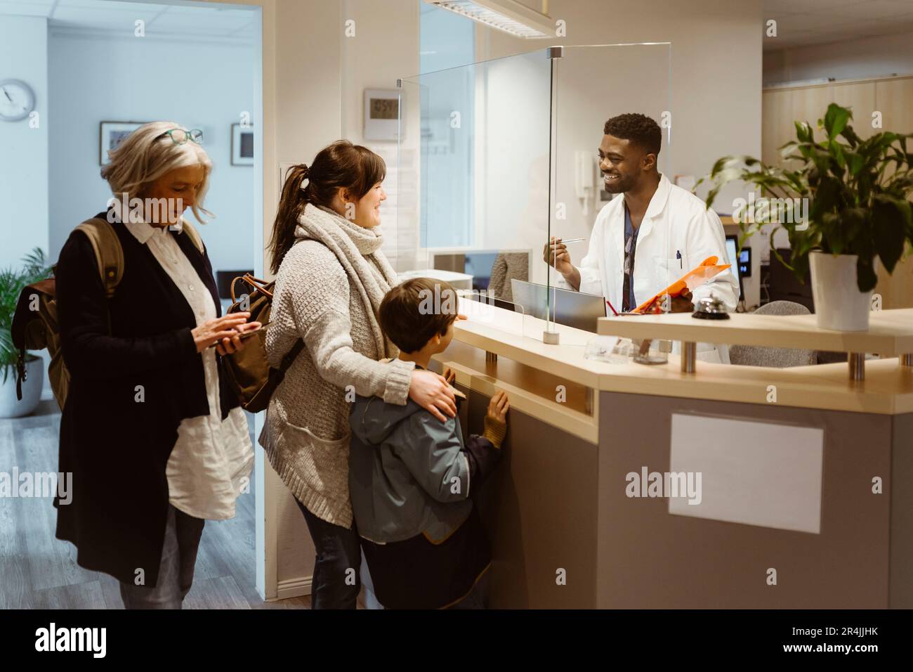 Patients standing and talking to male receptionist through transparent ...
