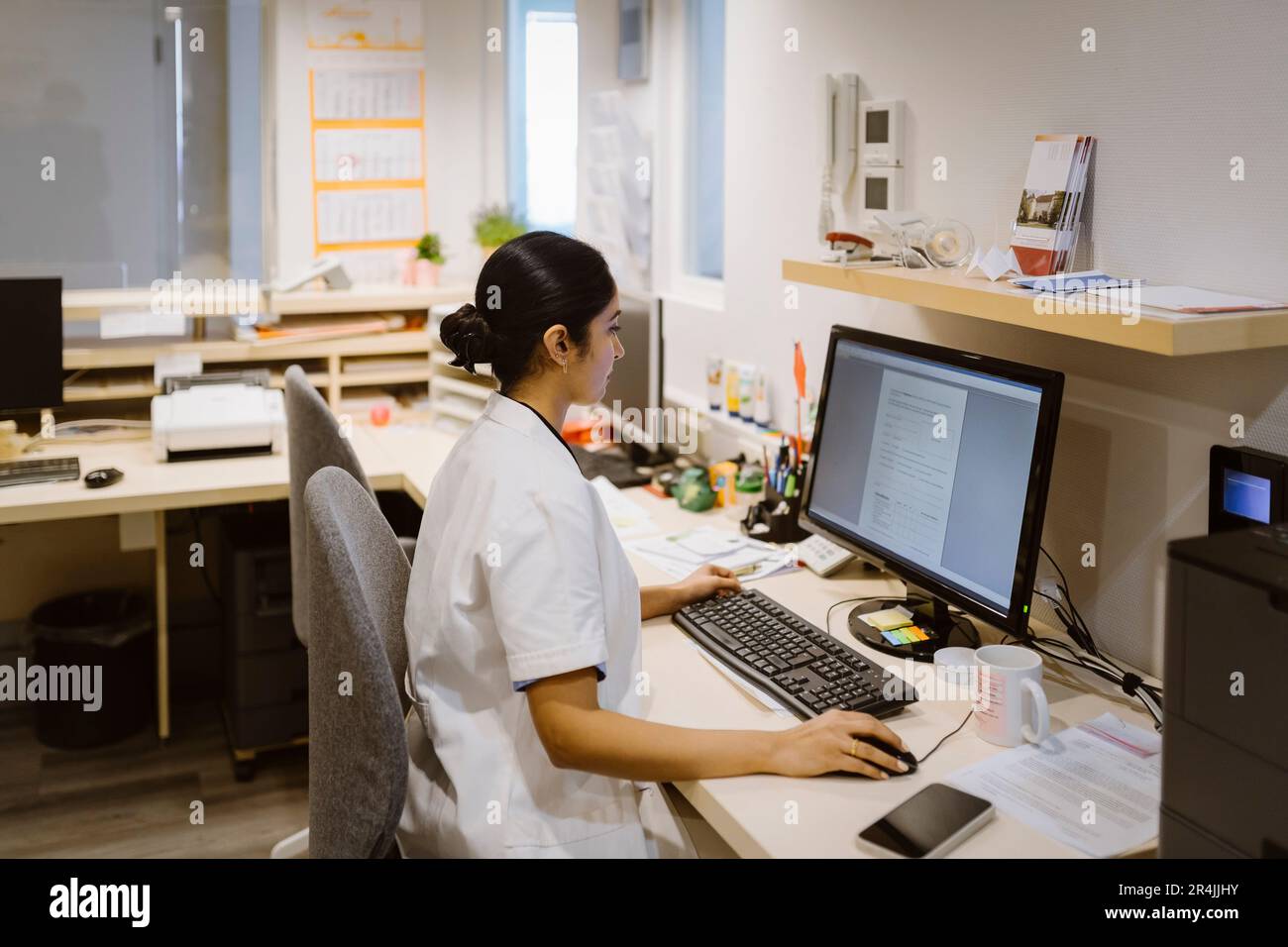 Side view of female healthcare worker using desktop PC at hospital ...