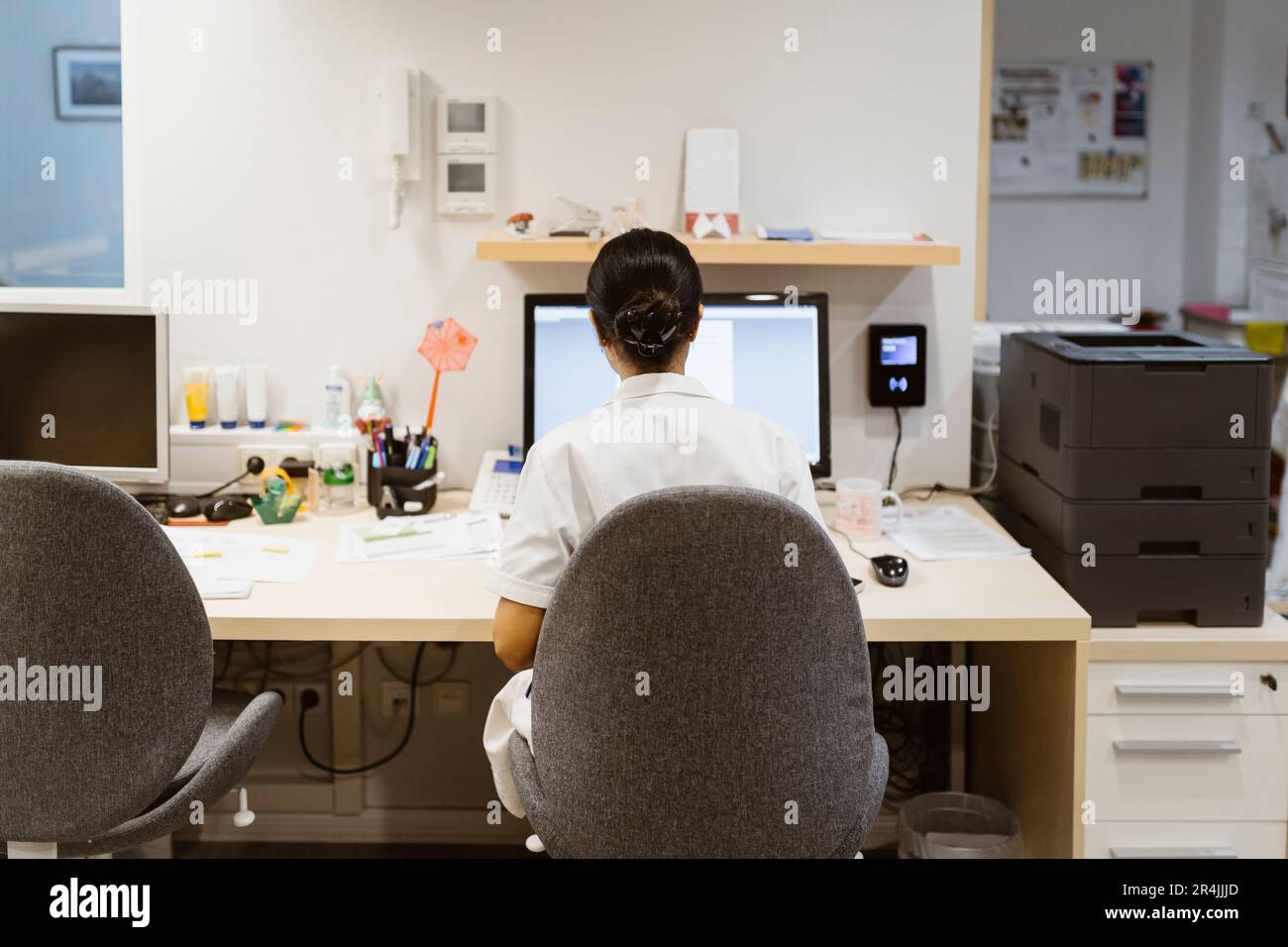 Rear view of female doctor working on desktop computer while sitting on ...