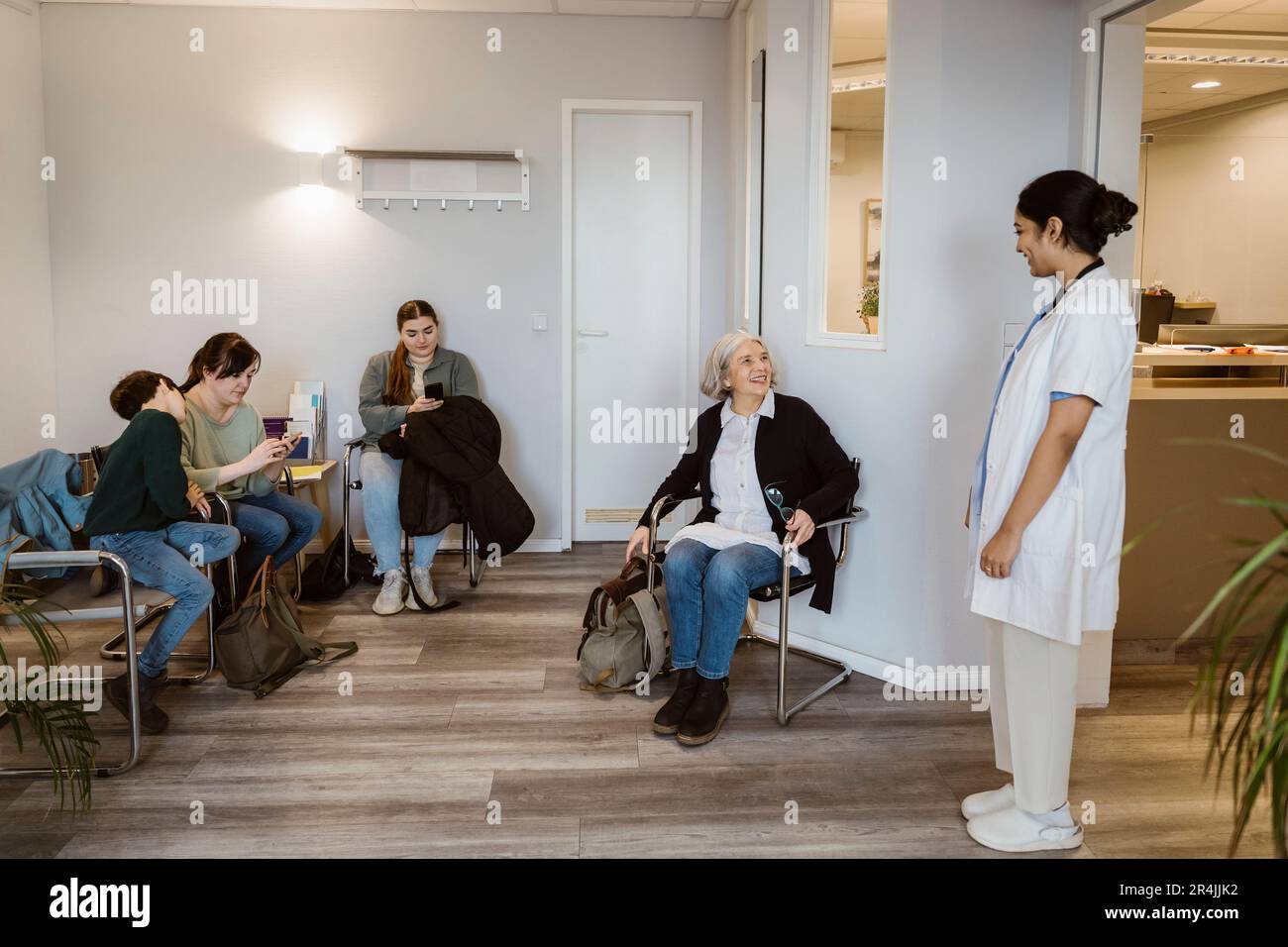 Female healthcare worker communicating with patients sitting in waiting room at healthcare ...