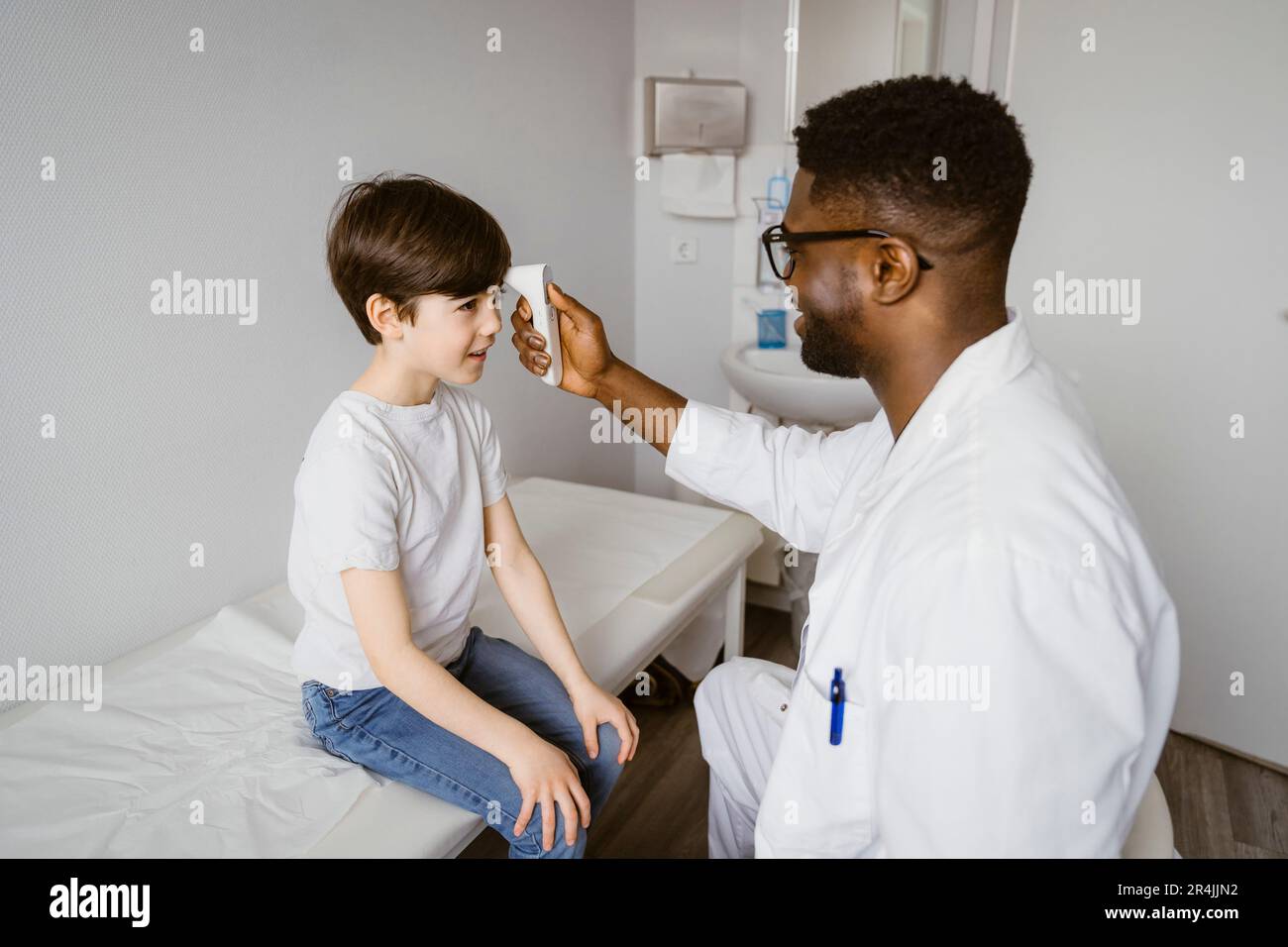 Young male pediatrician measuring temperature of boy using infrared ...