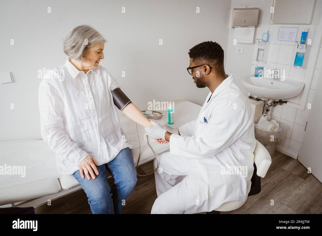 Young male doctor checking blood pressure of female patient at clinic ...