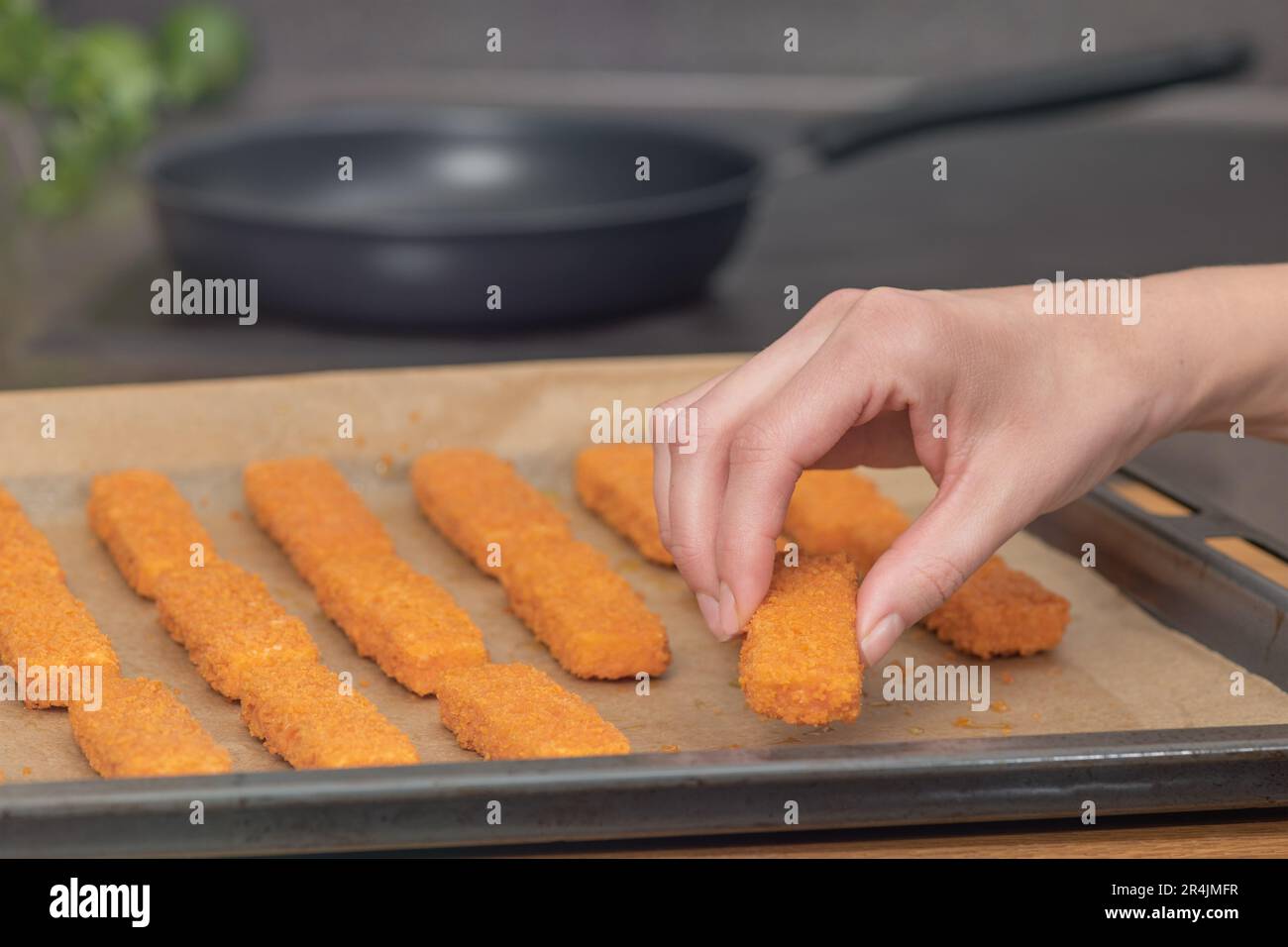 The hand lays out fish fingers against the background of a frying pan ...