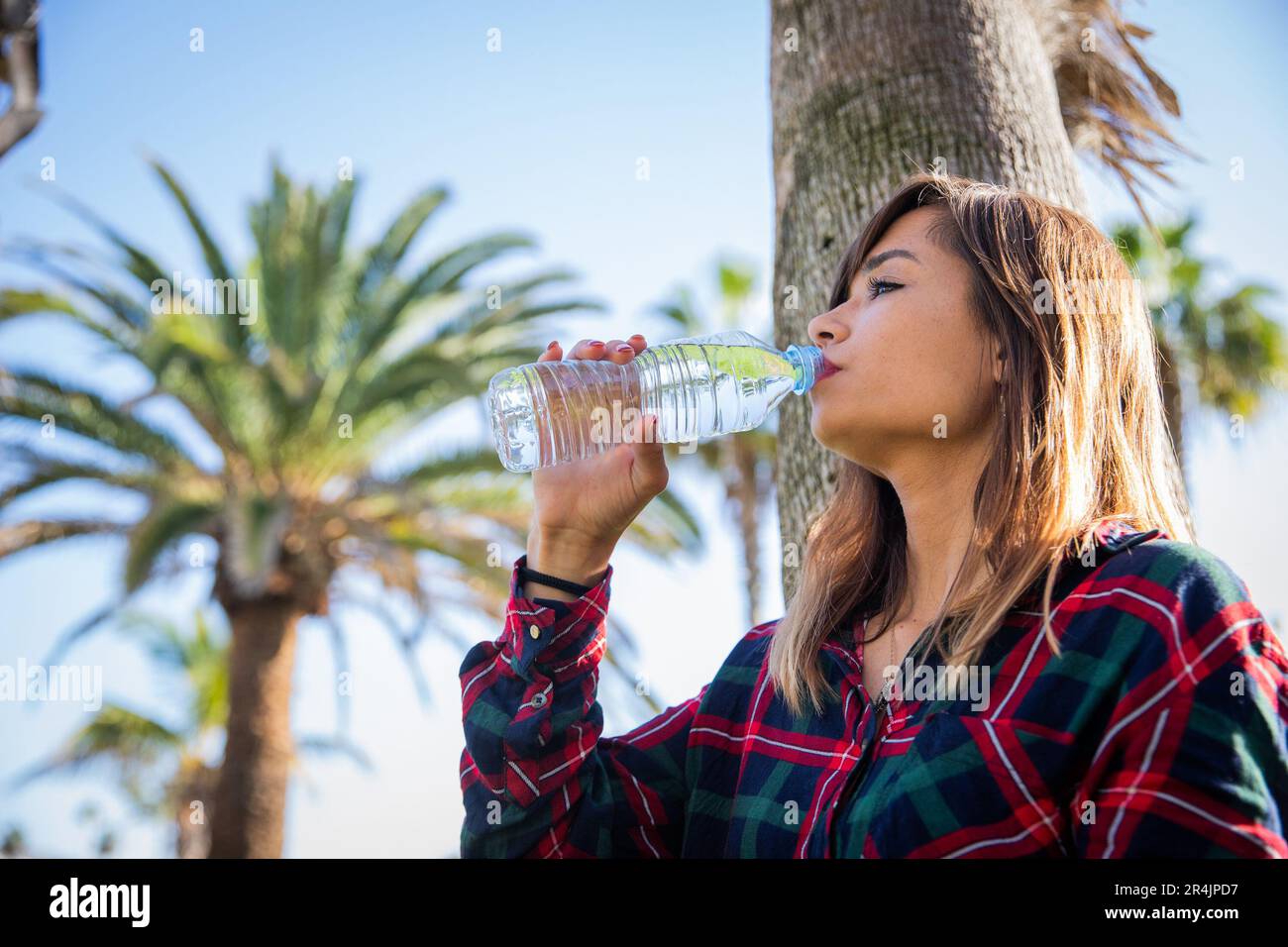 A girl drinks some water while standing outside in a tropical park ...