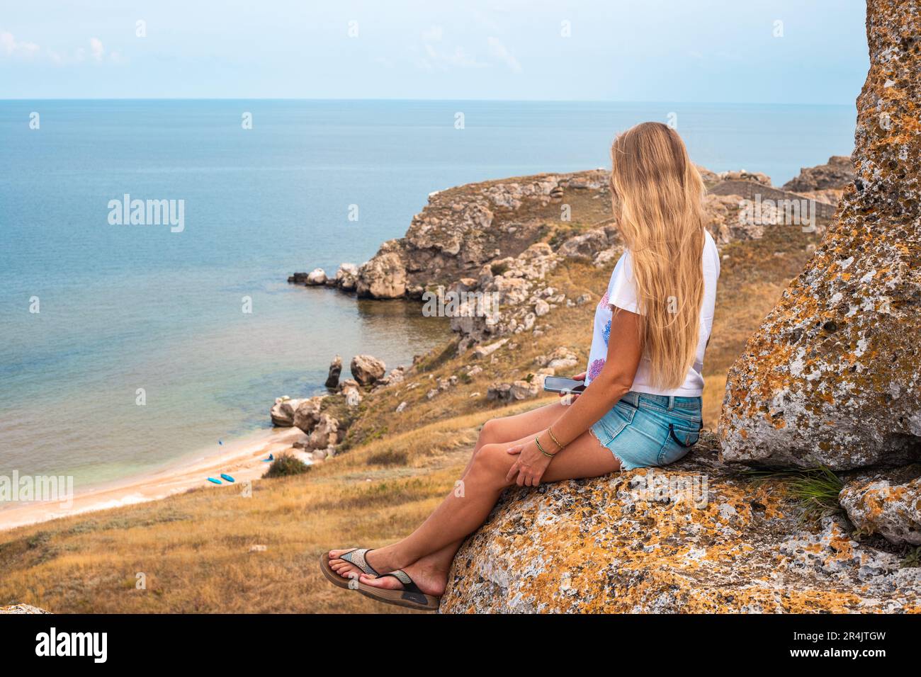 A woman with long blond hair sits on top of a mountain and looks down ...