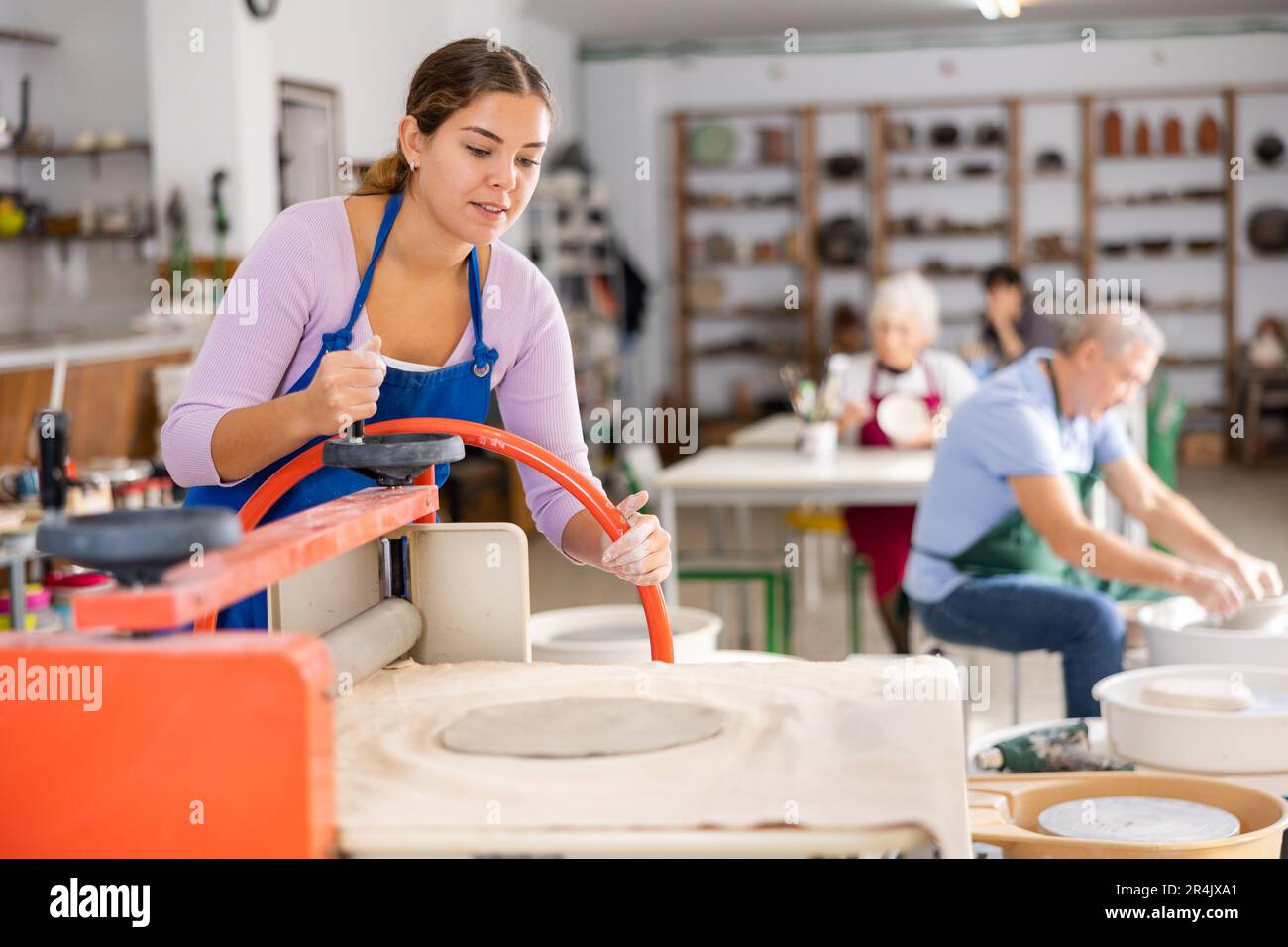 Young woman rolls out clay on craft machine clay press roller in studio ...