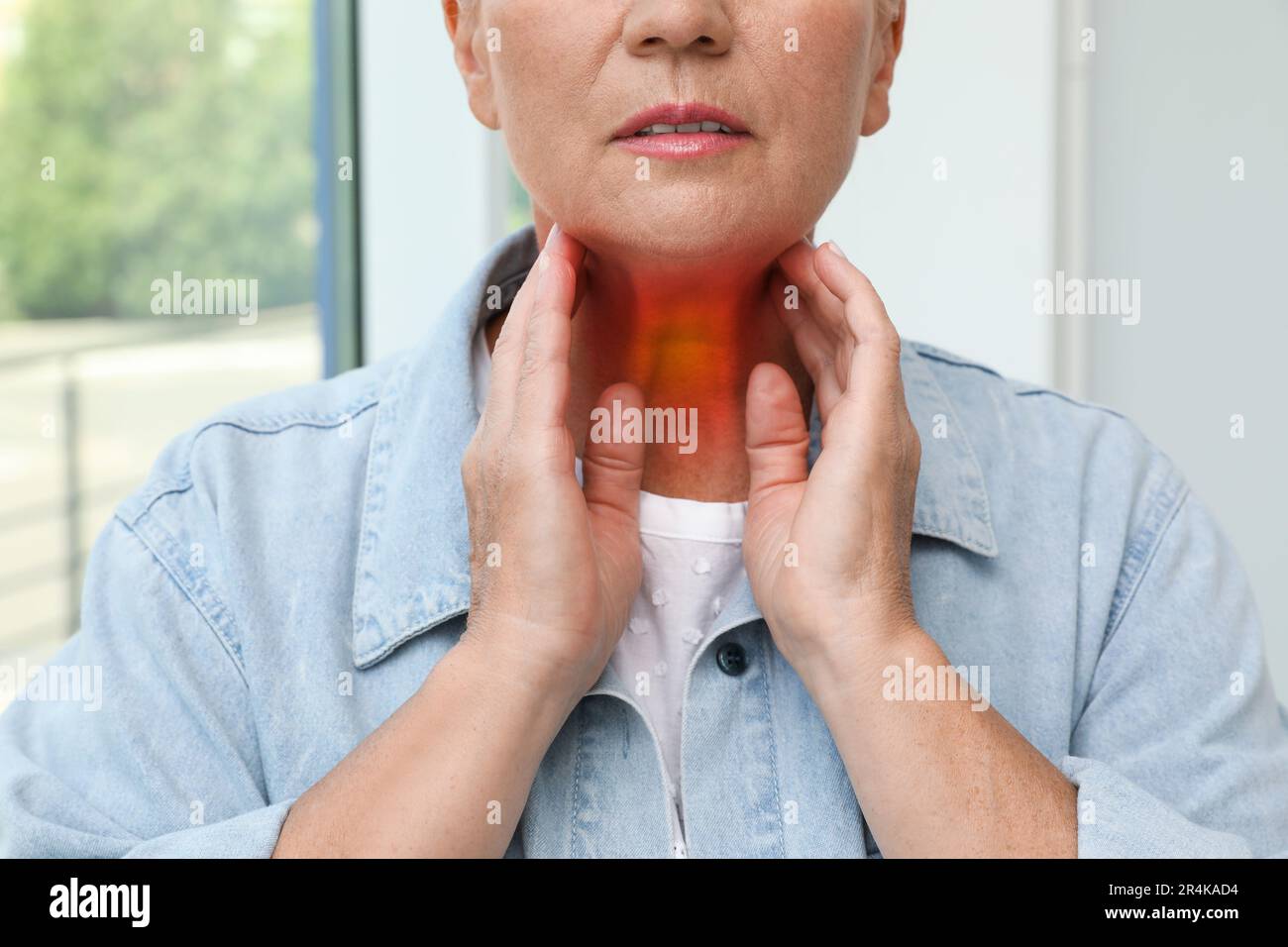 Endocrine system. Mature woman doing thyroid self examination indoors ...