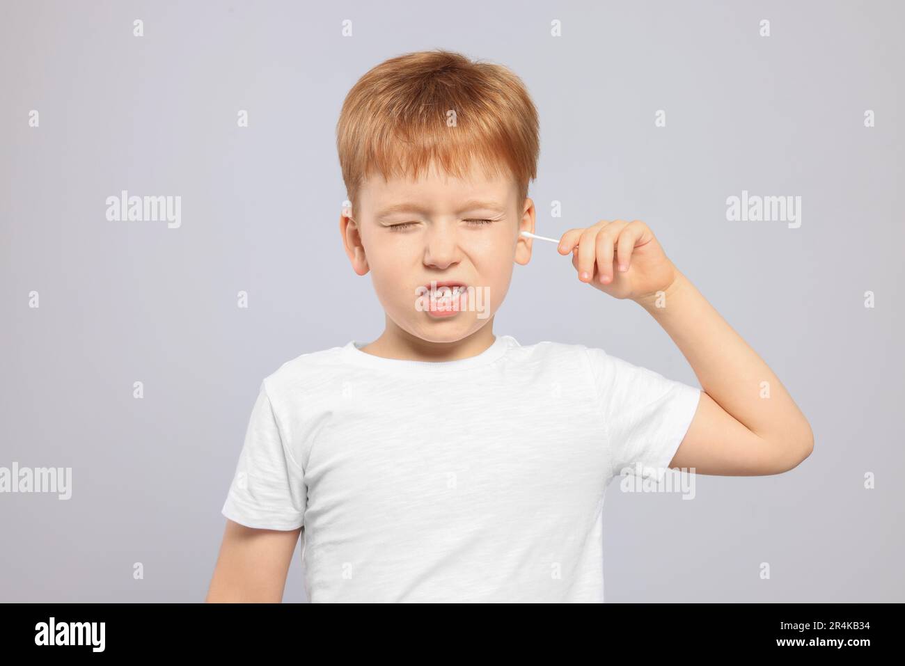 Little boy cleaning ear with cotton swab on light grey background Stock ...