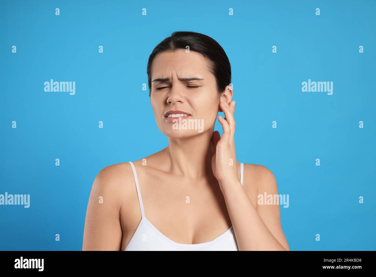 Young woman suffering from ear pain on light blue background Stock ...