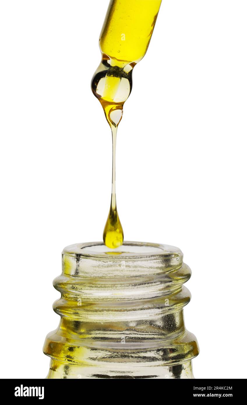 Dripping yellow facial serum from pipette into glass bottle on white ...