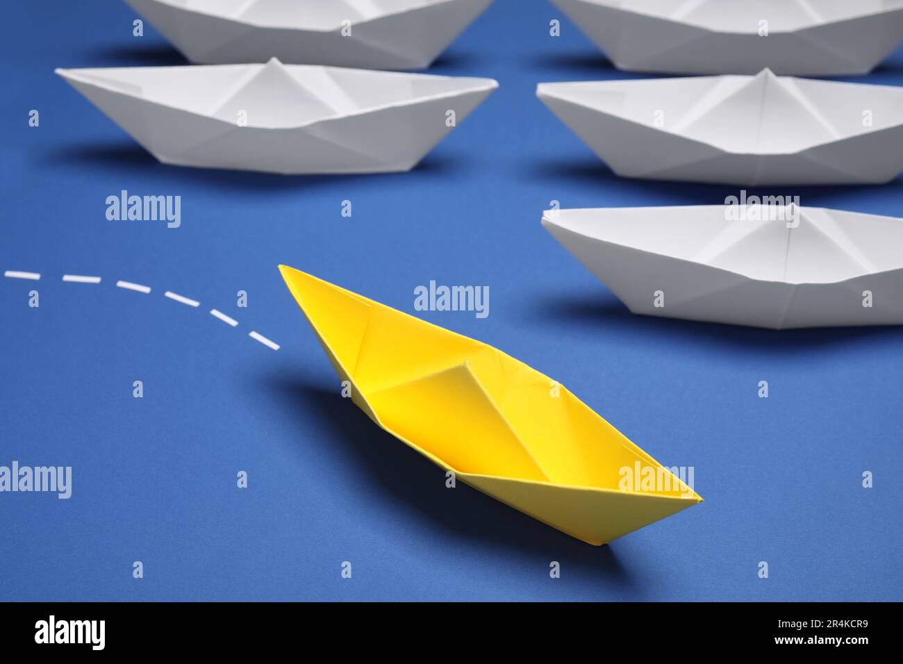 Yellow paper boat floating away from others on blue background, closeup ...
