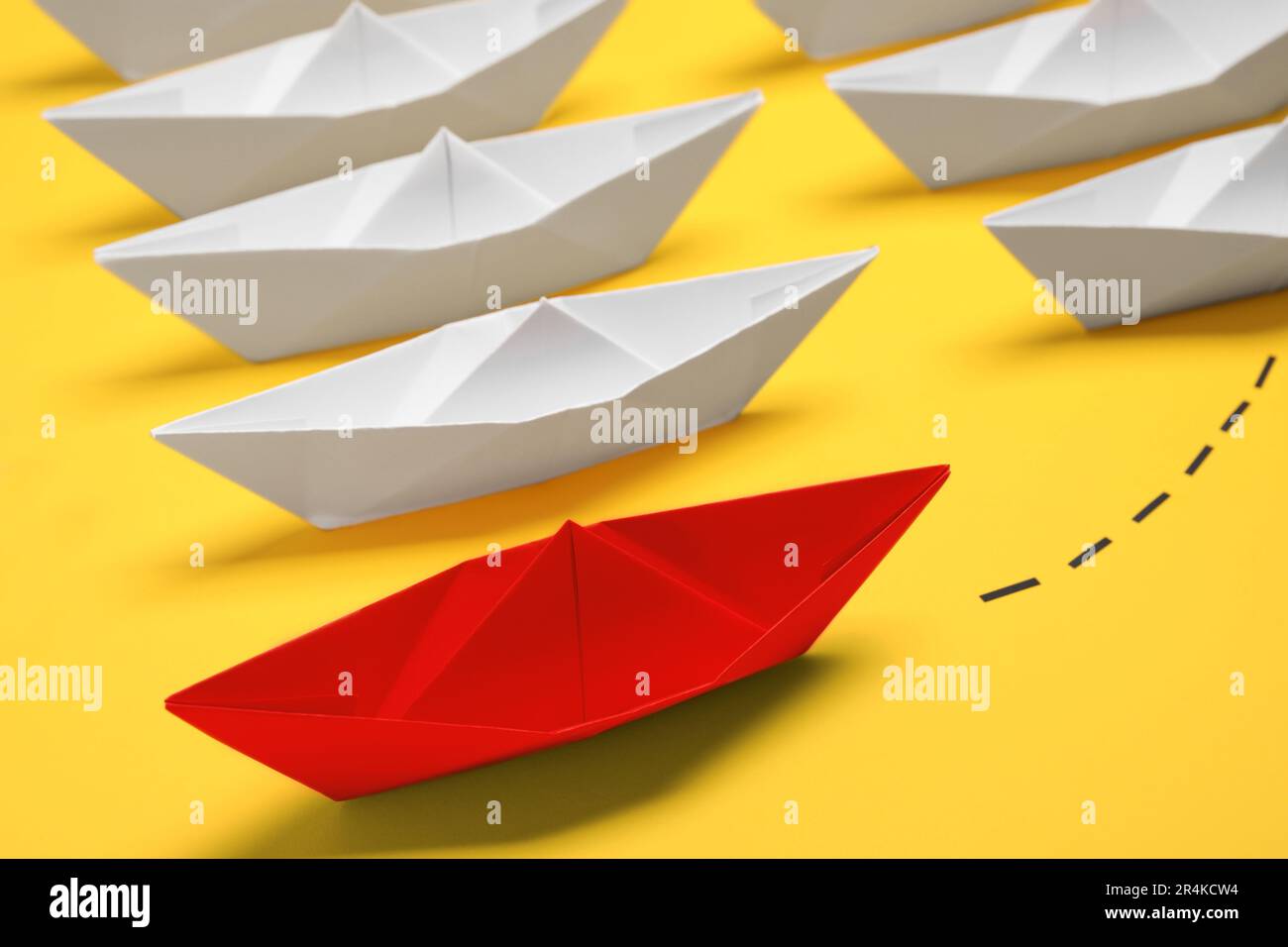 Red paper boat floating away from others on yellow background, closeup ...