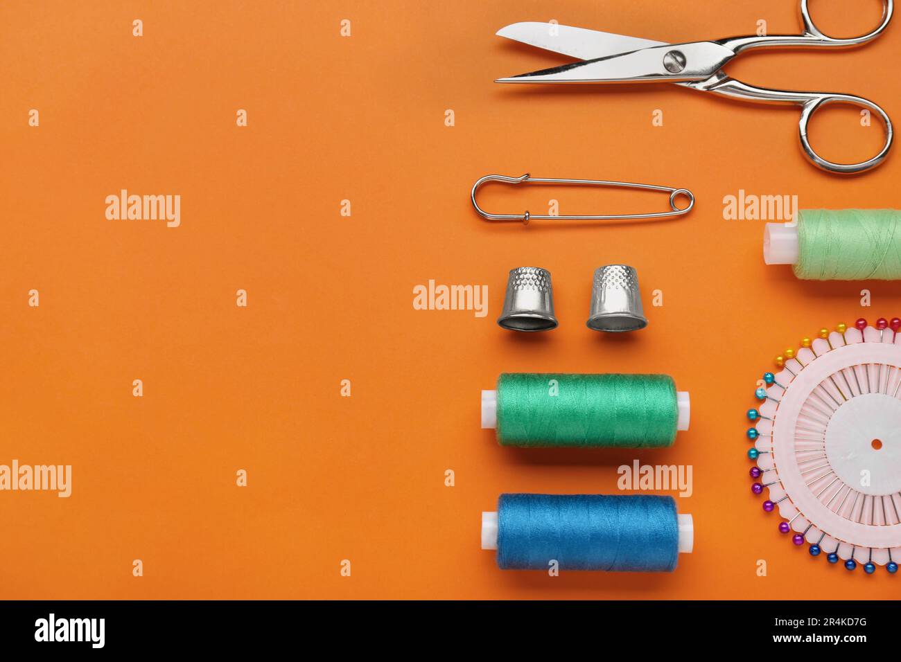 Flat lay composition with thimbles and different sewing tools on orange ...