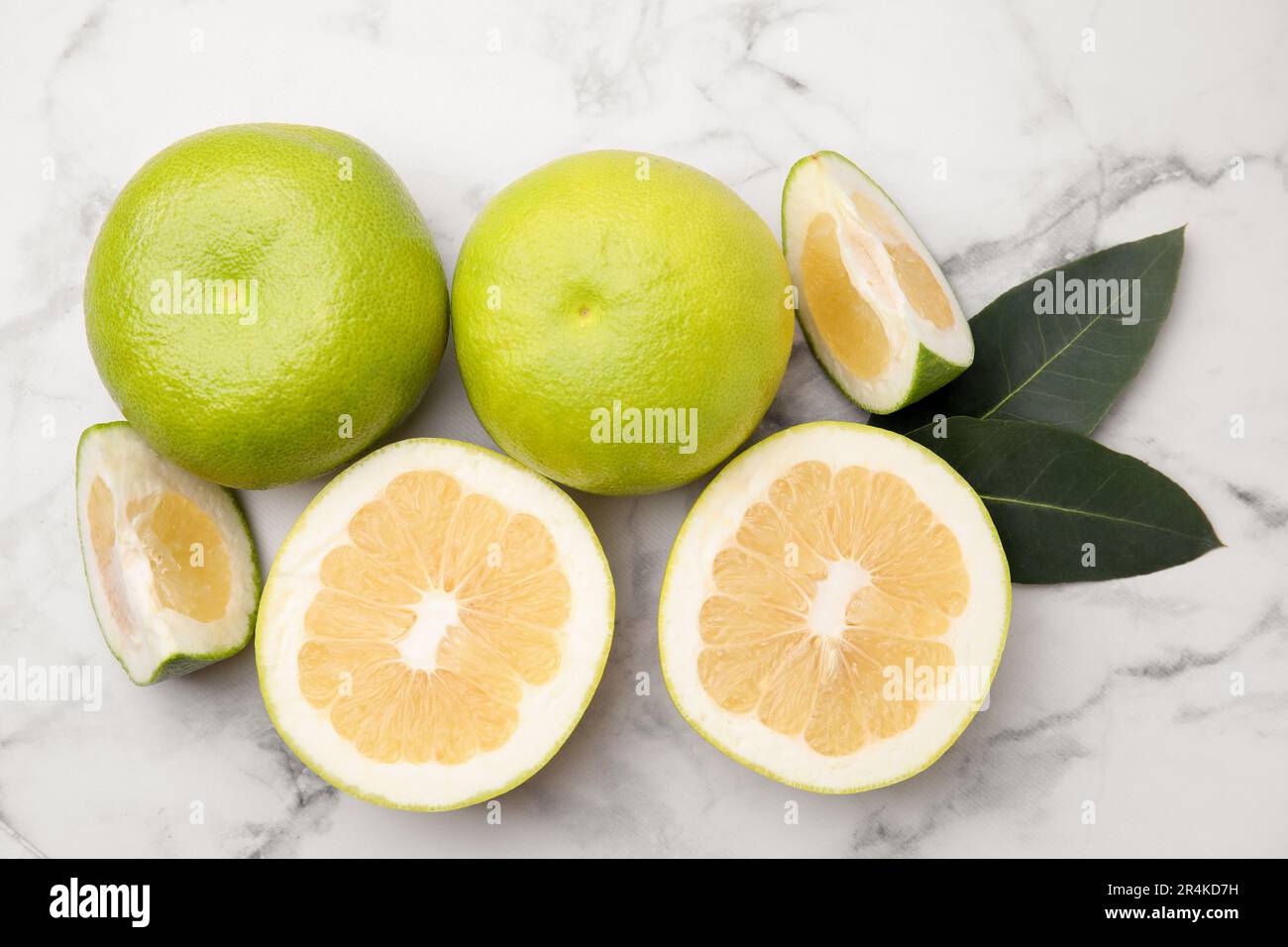 Whole and cut sweetie fruits with green leaves on white marble table ...