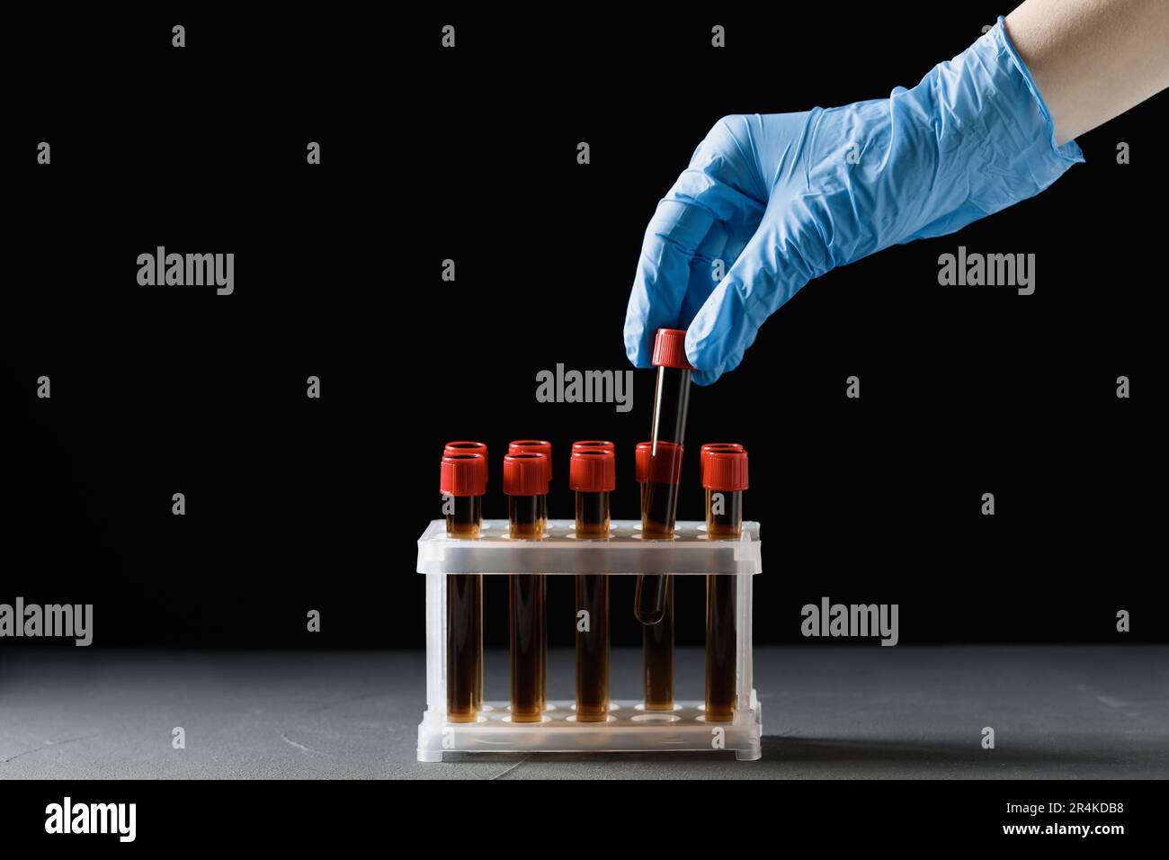 Scientist putting test tube with brown liquid into stand at grey table ...