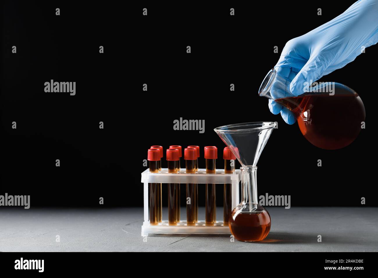 Scientist pouring brown liquid into flask at grey table against black ...