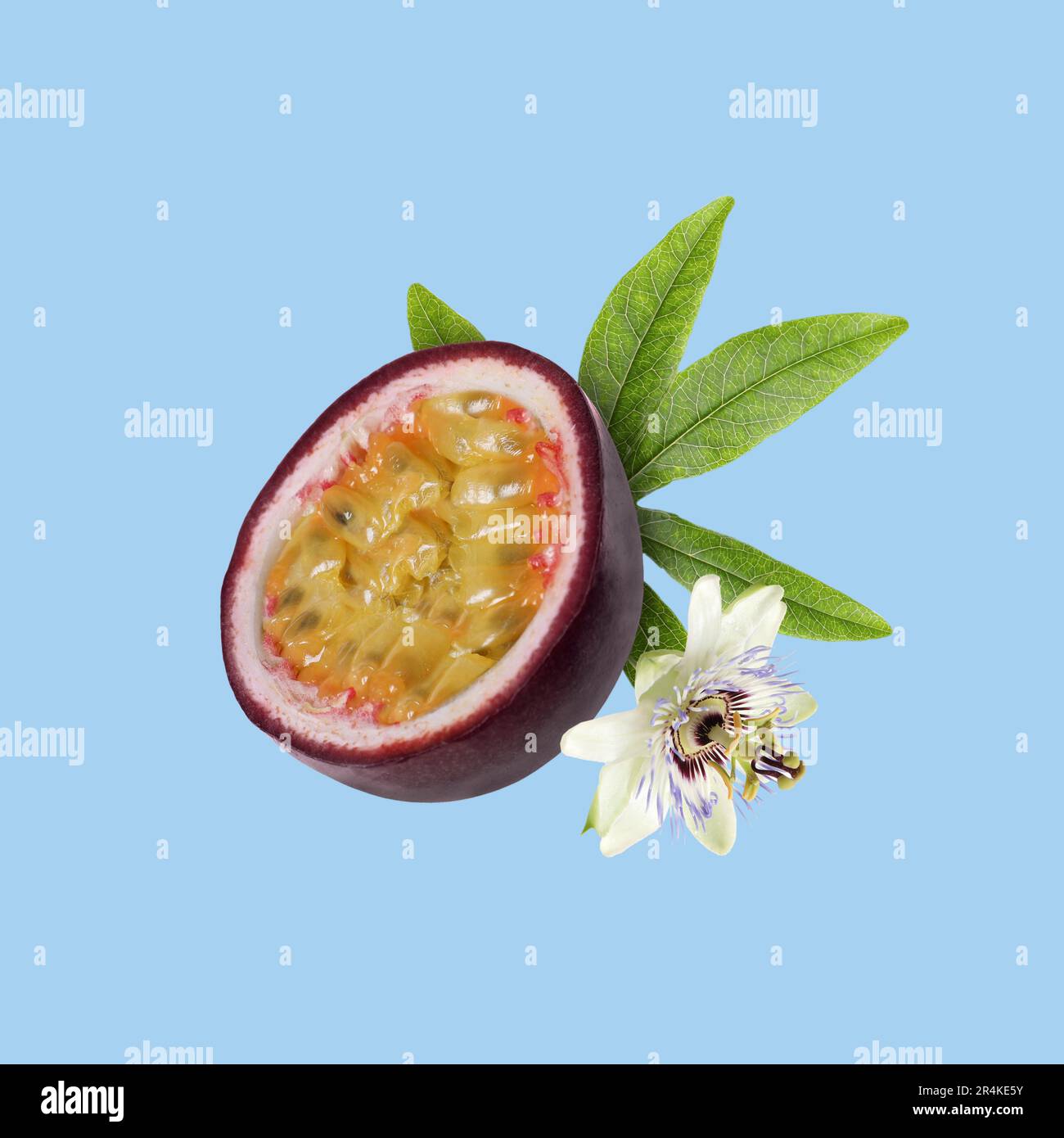 Half of passion fruit, leaf and passiflora flower falling on light blue ...