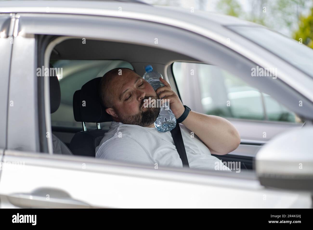Exhausted overweight man with close eyes after drive inside car bottle ...