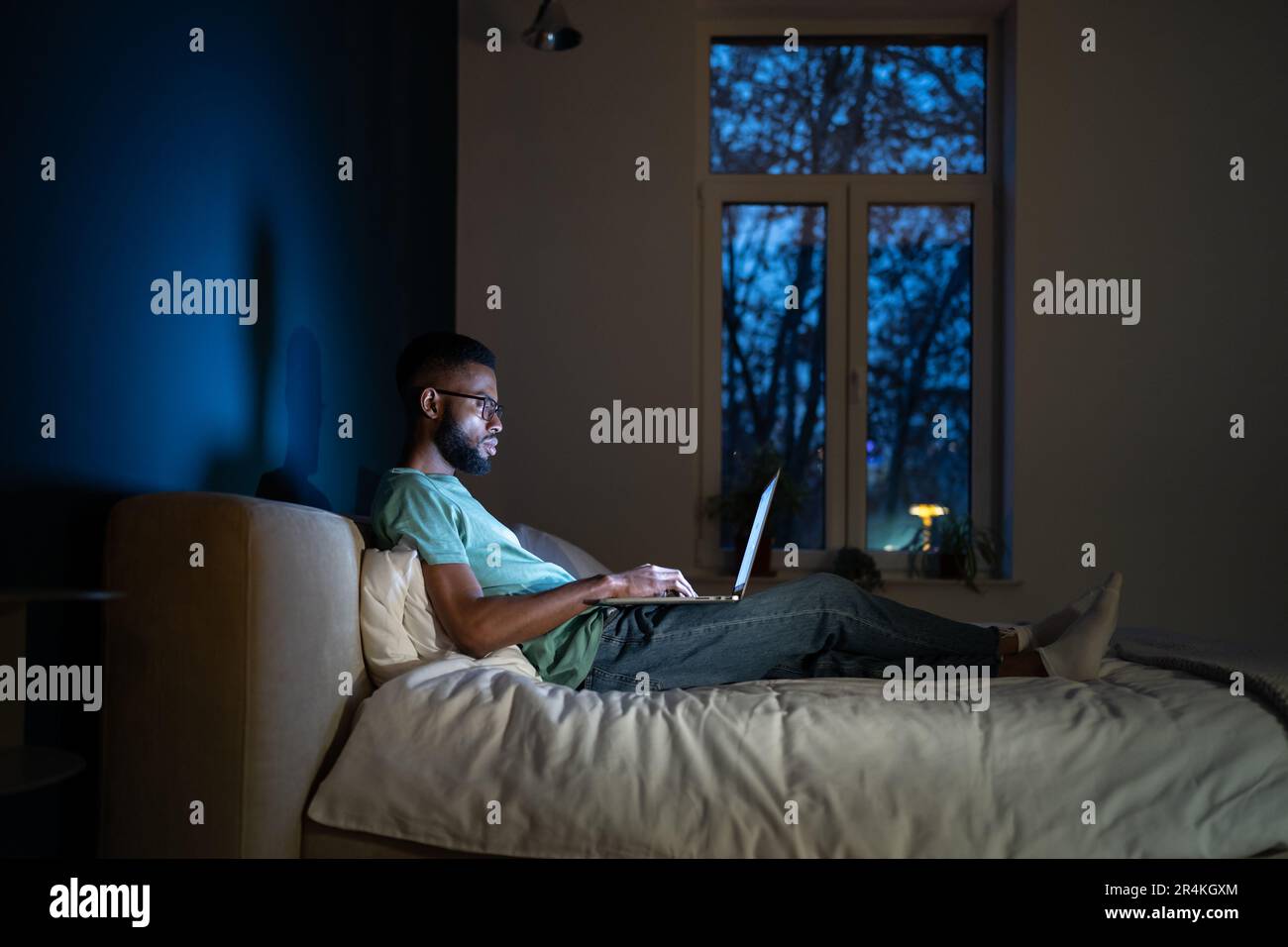 Concentrated African American programmer man lying on bed work on ...
