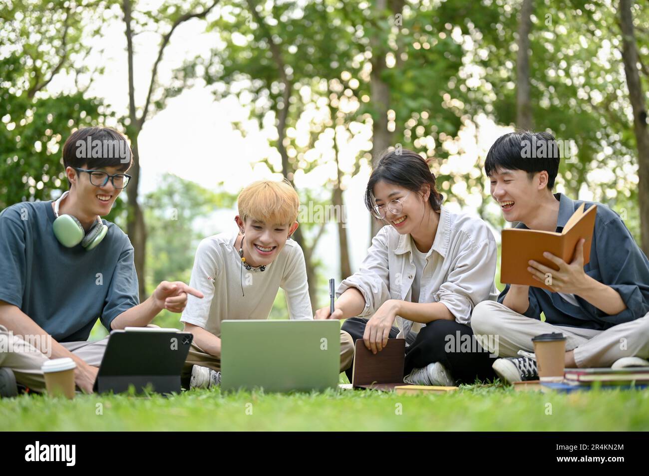 A group of diverse young Asian college students sitting on the grass enjoy talking, sharing ...