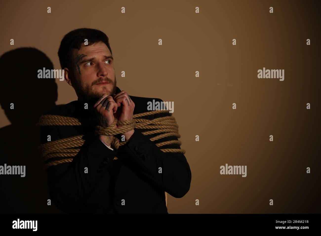 Scared man tied up and taken hostage on dark background. Space for text ...