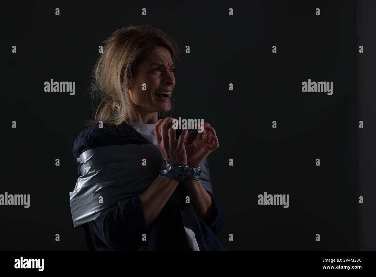 Scared woman taped up and taken hostage on dark background. Space for ...