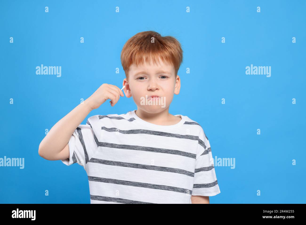 Little boy cleaning ear with cotton swab on light blue background Stock ...