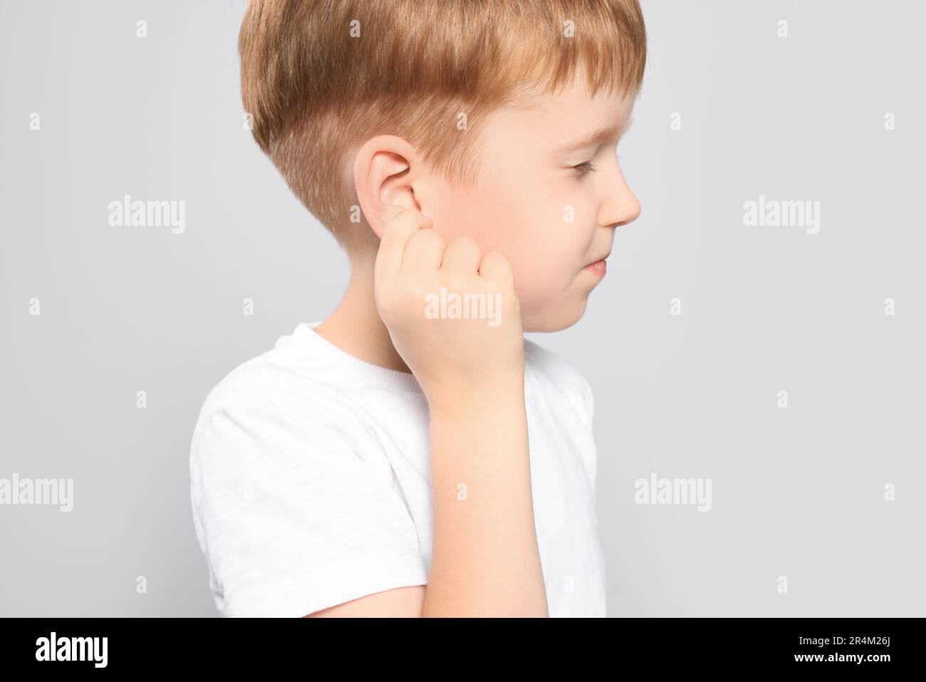 Little boy suffering from ear pain on light grey background, closeup ...