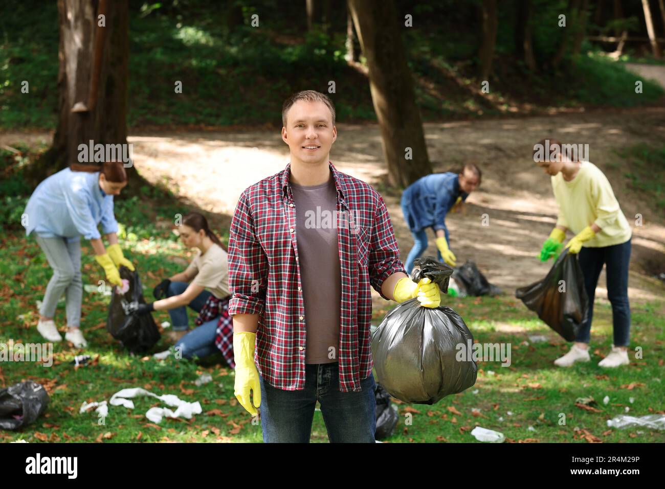 Young man with plastic bag and group of people collecting garbage in ...