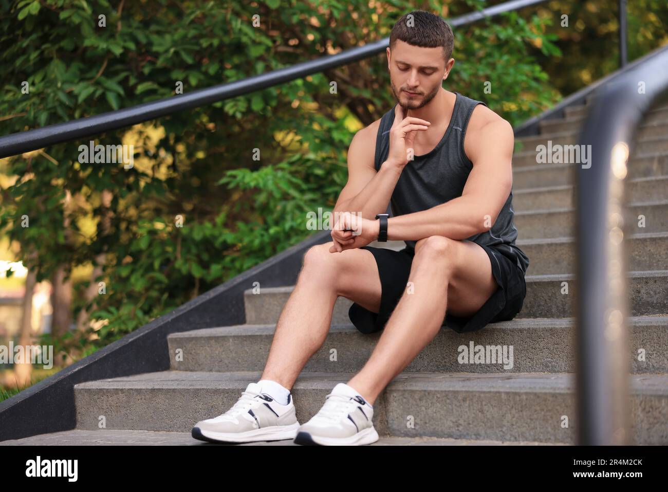 Attractive serious man checking pulse after training on stairs in park ...
