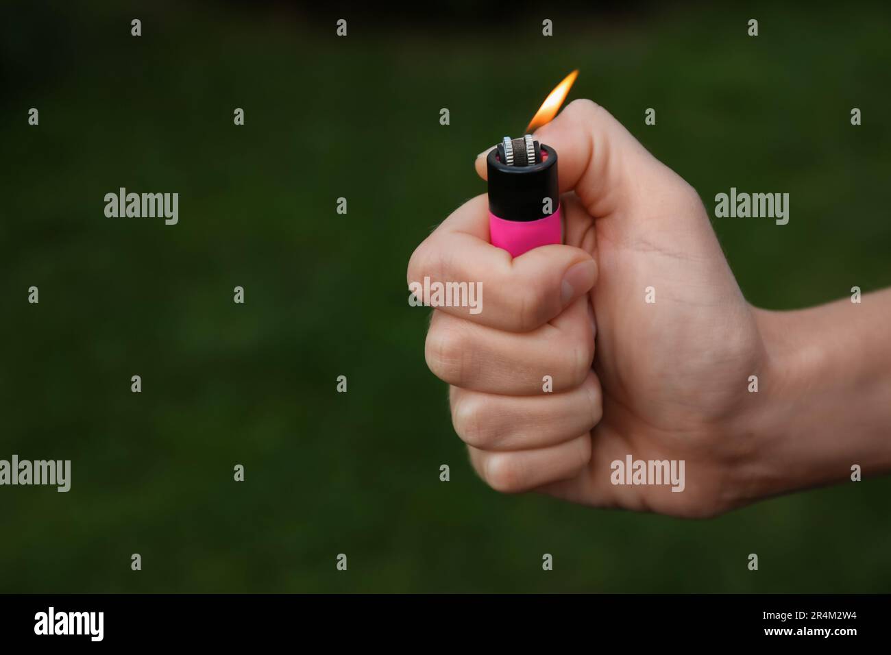 Man holding lighter with burning flame outdoors, closeup. Space for ...