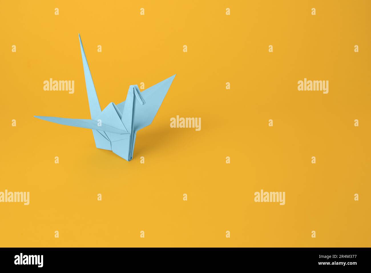 Origami art. Beautiful light blue paper crane on orange background ...