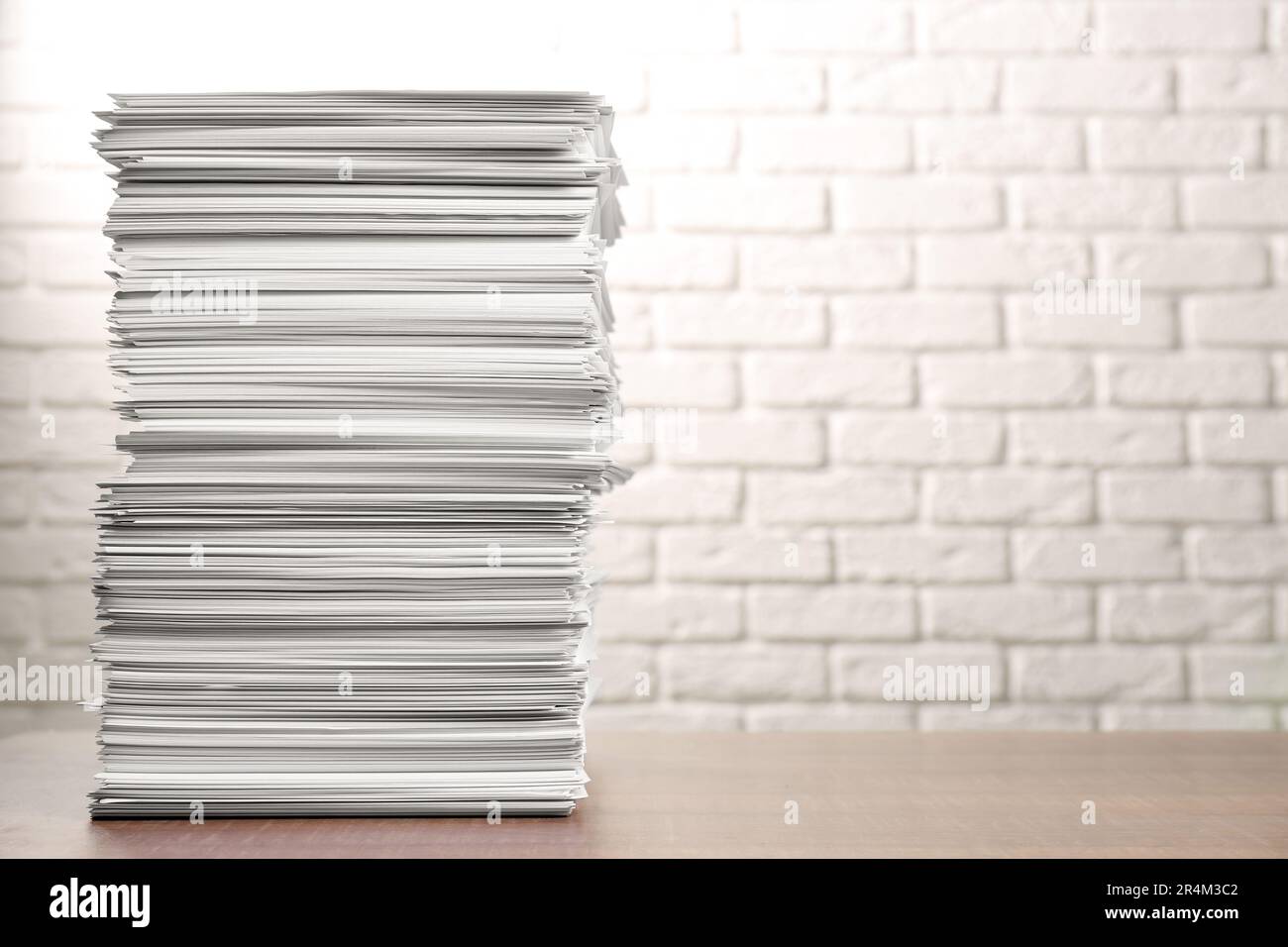 Stack of paper sheets on wooden table near white brick wall, space for ...