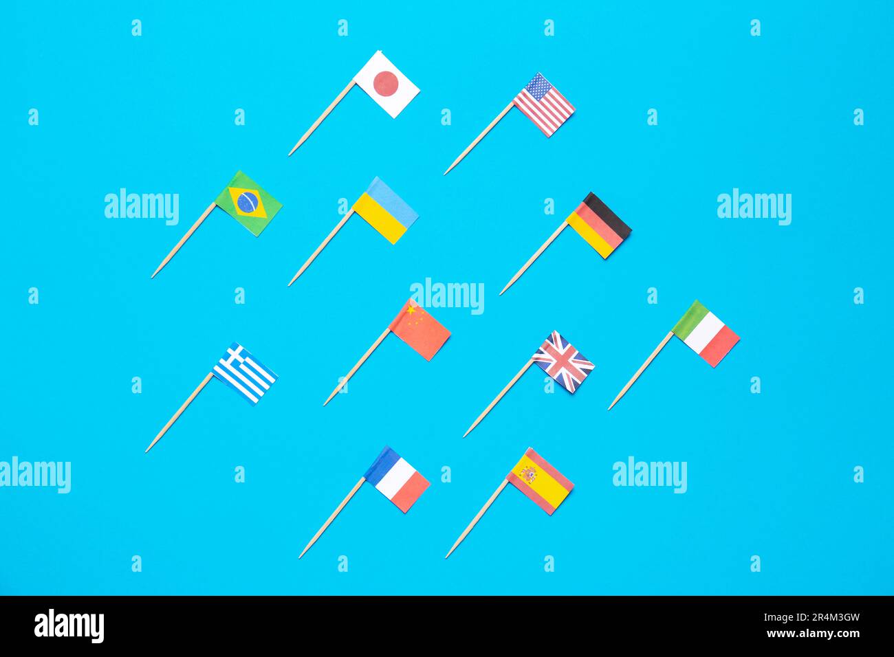 Many small paper flags of different countries on light blue background ...