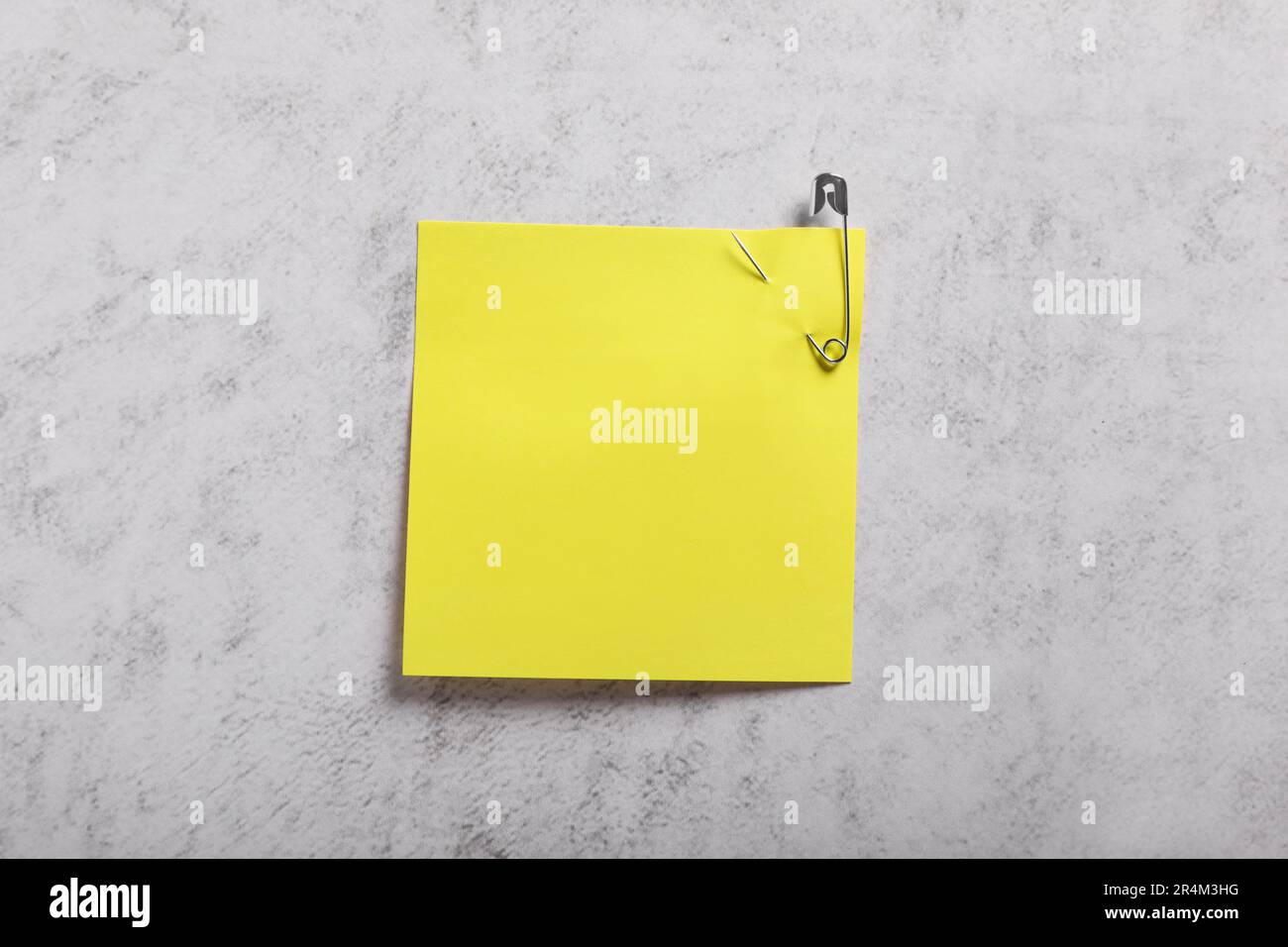 Yellow paper note with safety pin on grey textured background, top view ...