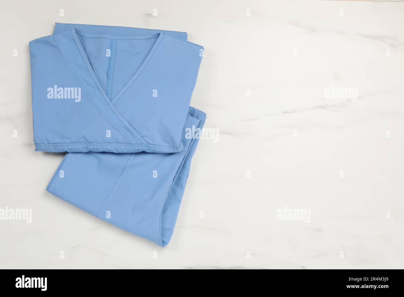 Light blue medical uniform on white marble table, top view. Space for ...