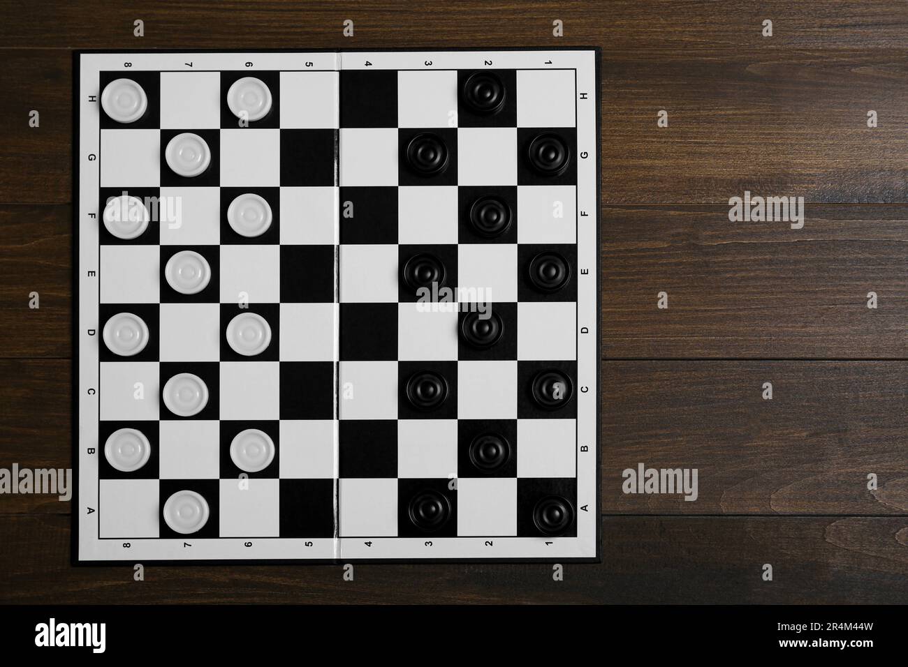 Checkerboard with game pieces on wooden table, top view. Space for text ...