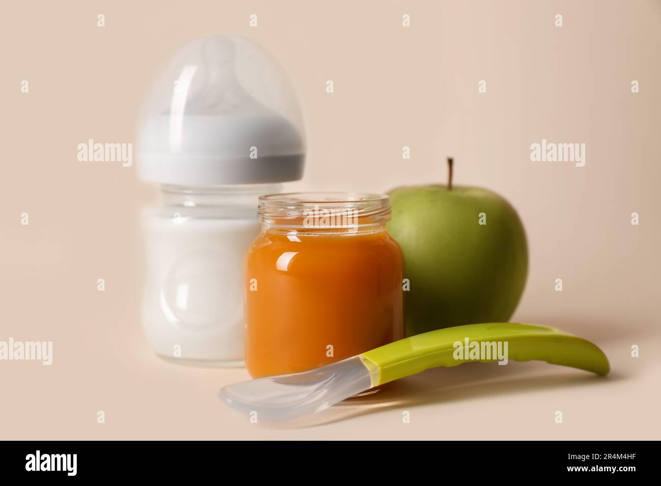 Healthy baby food in jar, bottle of milk, apple and spoon on beige ...