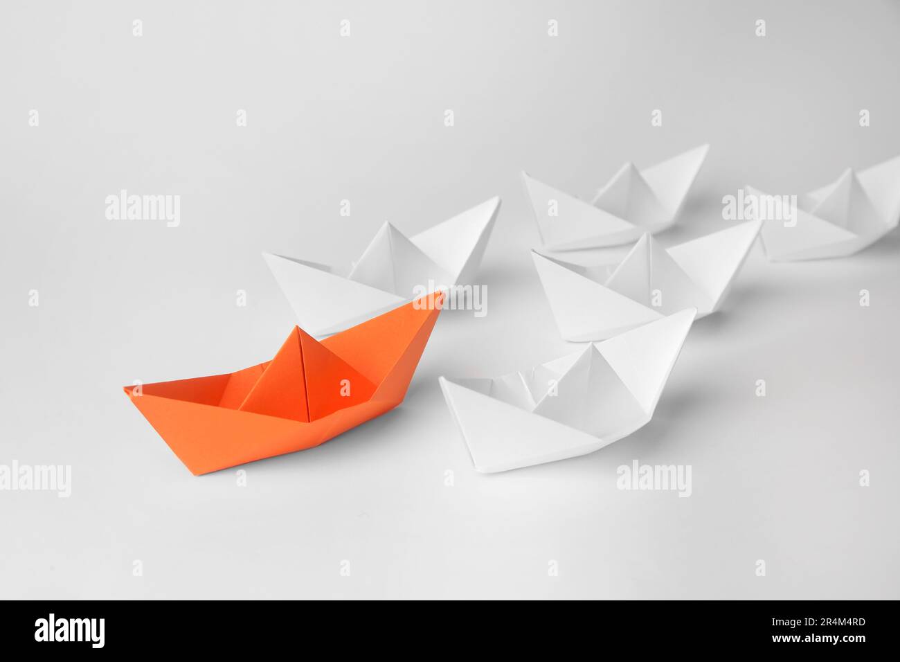 Group of paper boats following orange one on white background ...