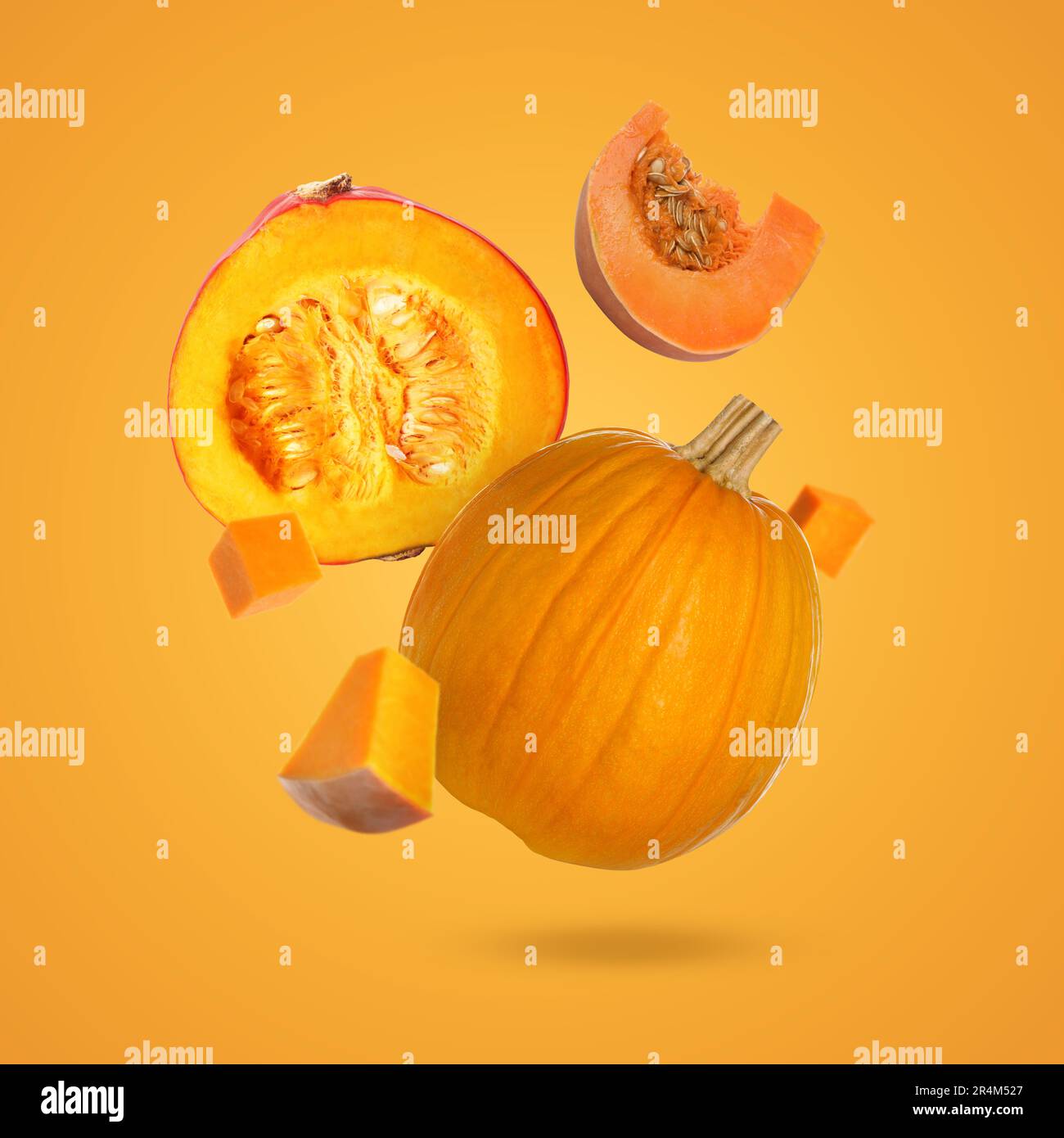 Whole and cut pumpkins falling on orange background Stock Photo - Alamy