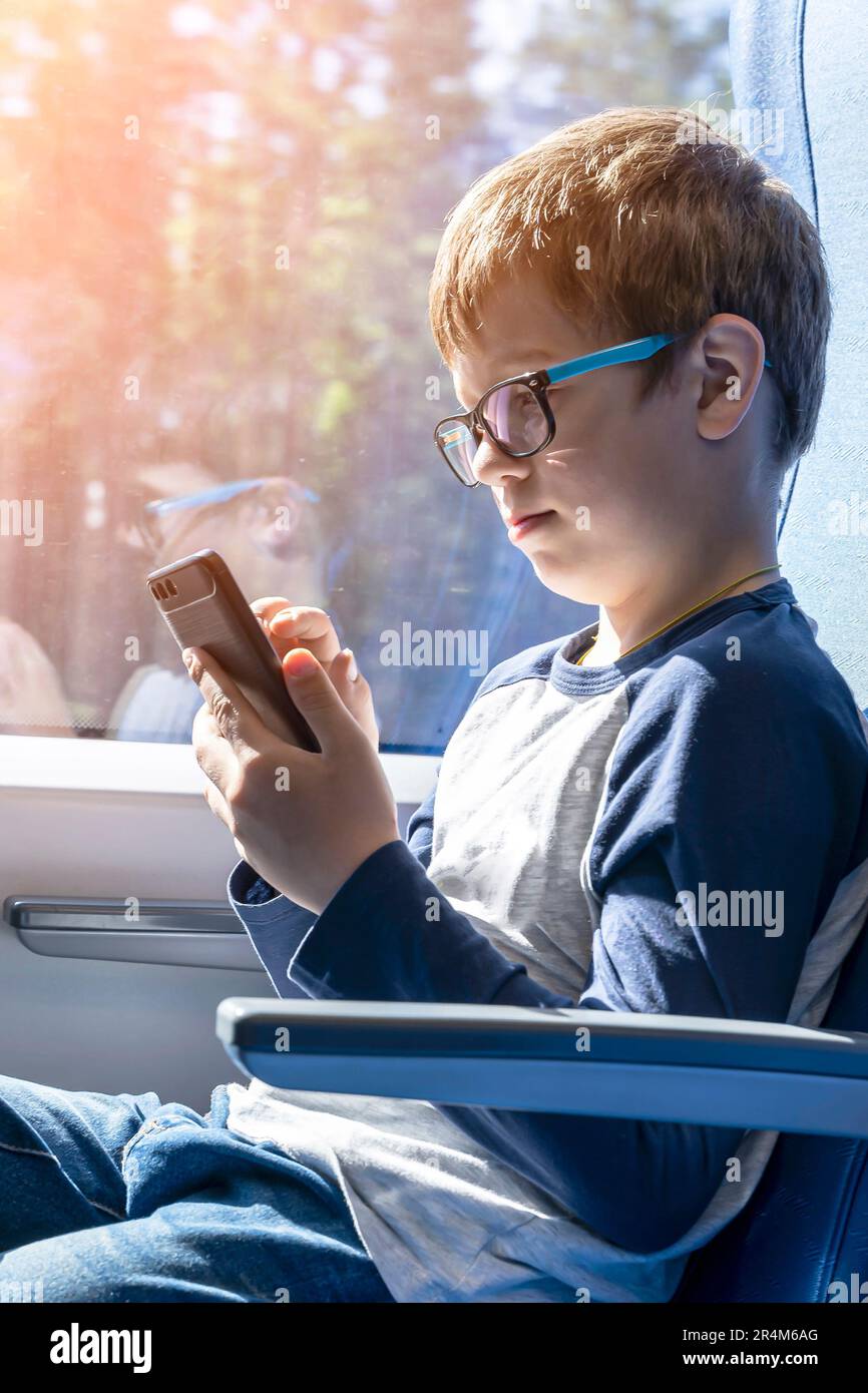 a cute Caucasian school-age boy with glasses rides a commuter train ...