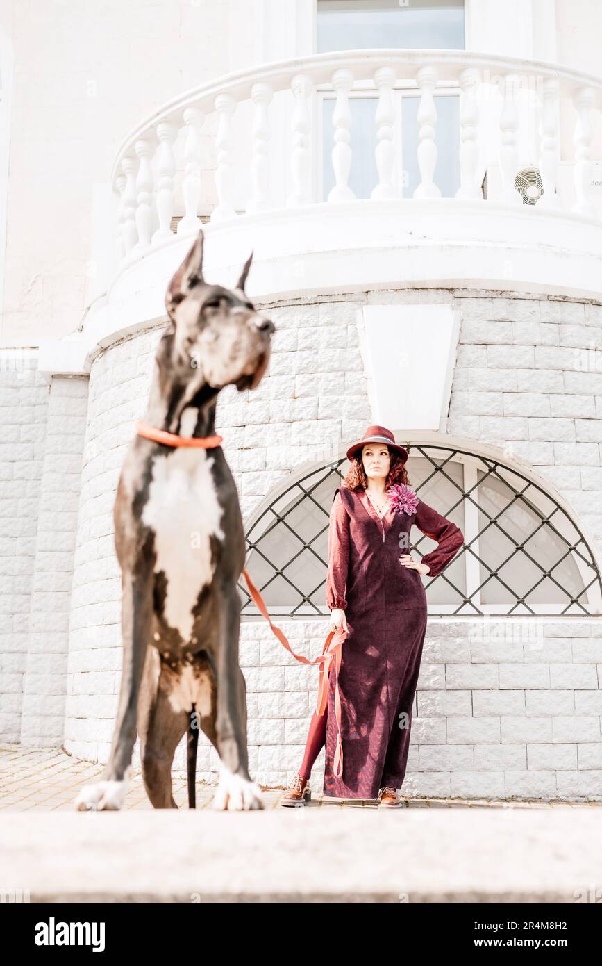 A photo of a woman and her Great Dane walking through a town, taking in ...
